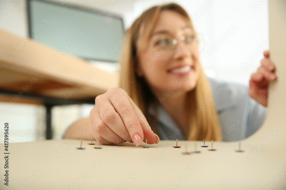 Young woman putting pins on colleague's chair in office. Funny joke ...