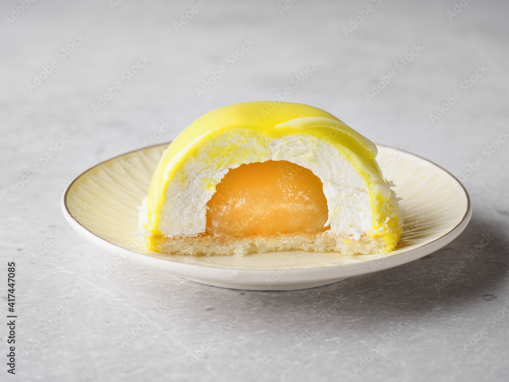 Yellow mousse cake cut in half on a light plate, grey background. Light ...