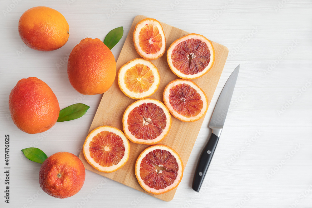 Red oranges whole and cut on a board and a knife, on a light background ...