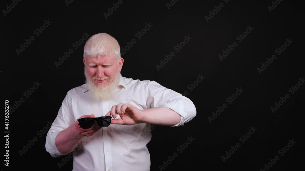 Vidéo Stock Man with albinism isolated on a black background raises his ...