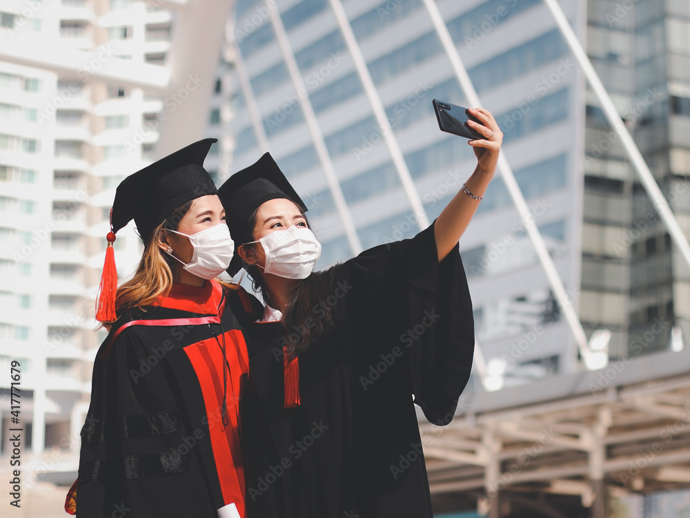 graduated women in graduation gowns and medical face masks, making ...