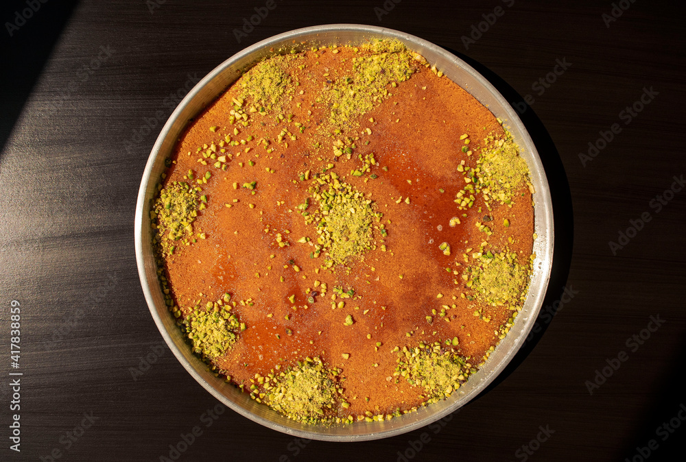 Eastern dessert kunafa in a big aluminium dish on dark black background ...