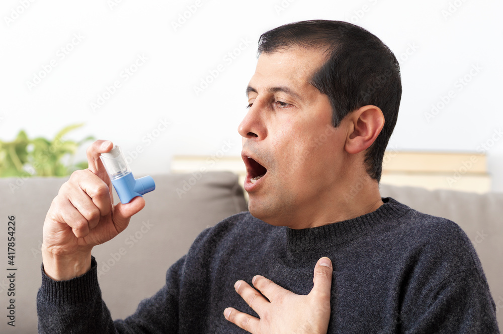 Man holding inhaler with asthma attack suffocating sitting on a couch ...