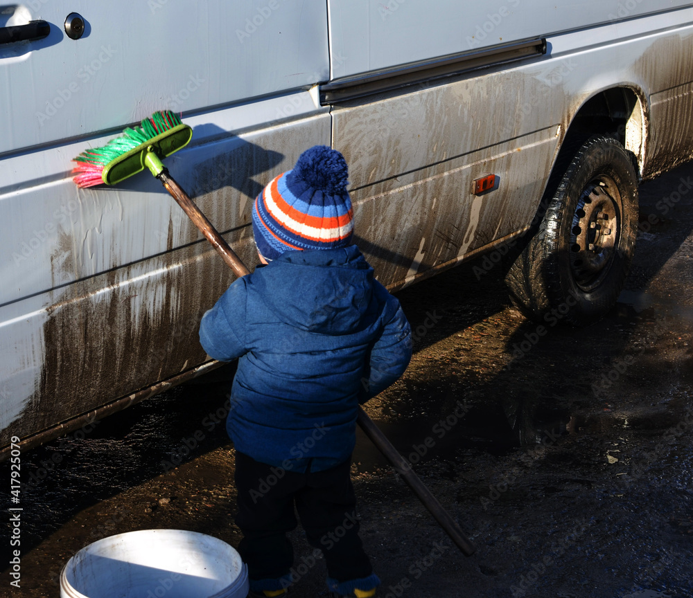 A little boy is cleaning a dirty car with a brush. The concept of child ...