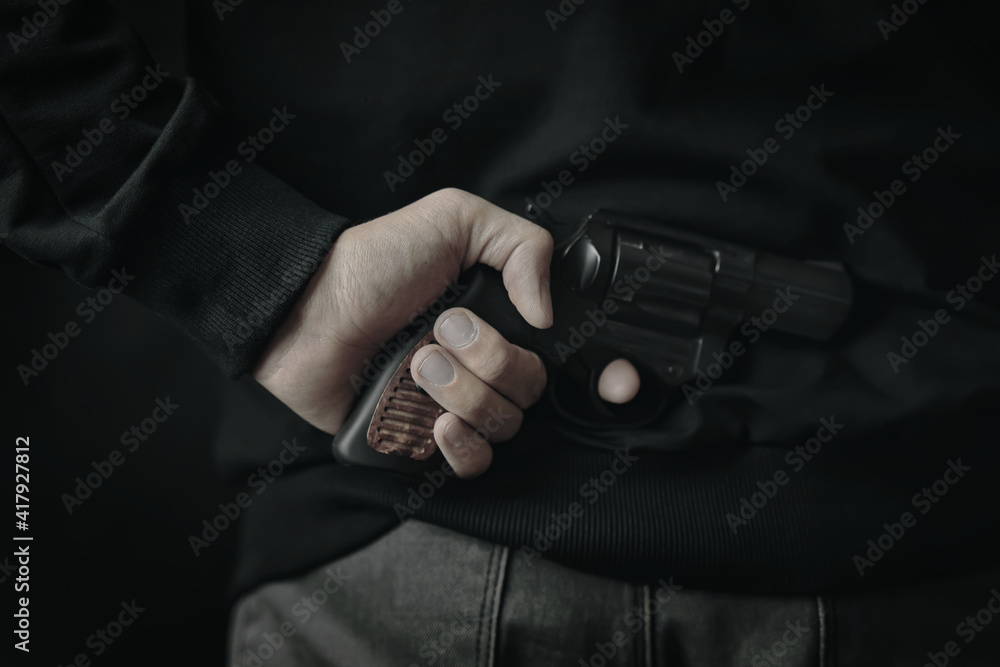 Man in grey cloth holds firearm behind his back. Revolver in men's hand ...