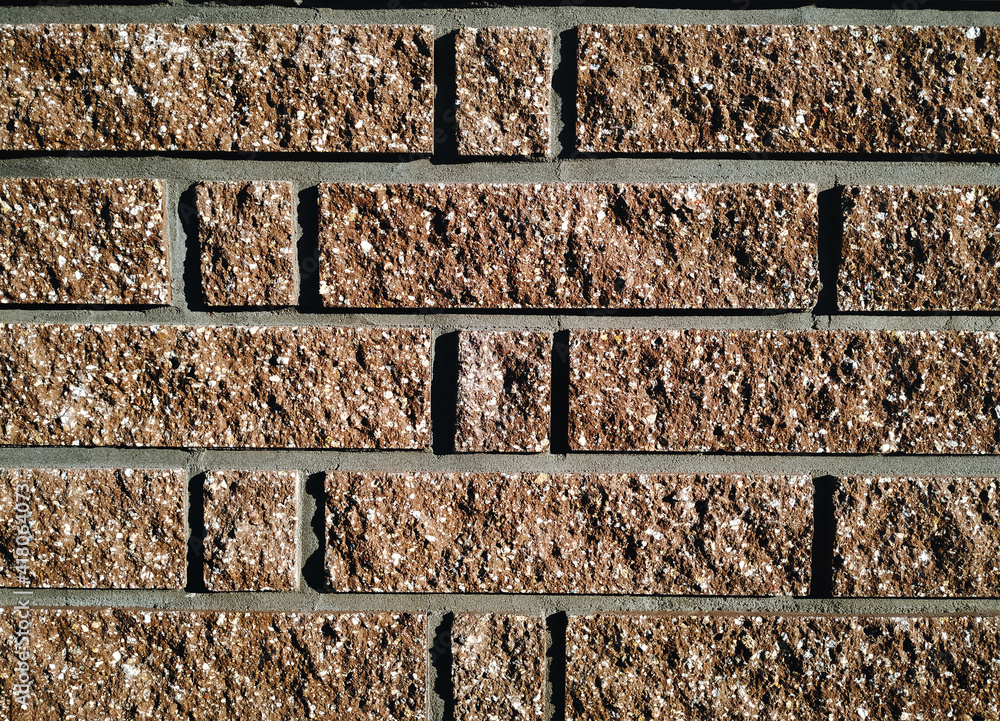 The texture of an old wall made of brown chipped decorative uneven bricks interspersed with ...
