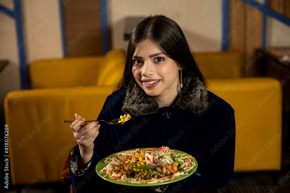 Portrait of a beautiful young Indian girl eating food while sitting in ...