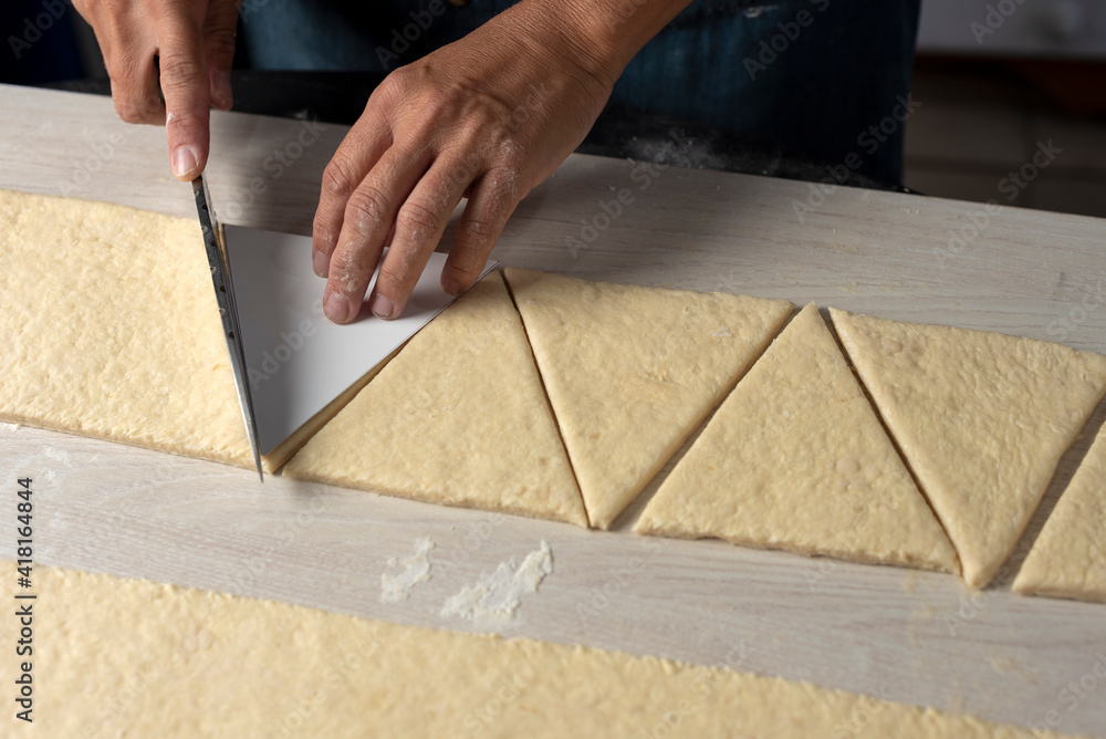 hands cutting the croissant dough with a knife and croissant into ...