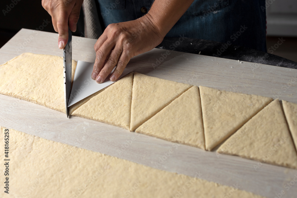 hands cutting the croissant dough with a knife and croissant into ...