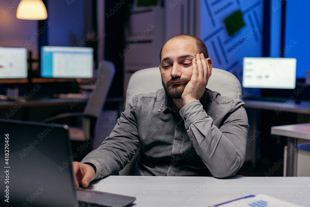 Bored sleepy businessman working on laptop doing overtime at workplace ...