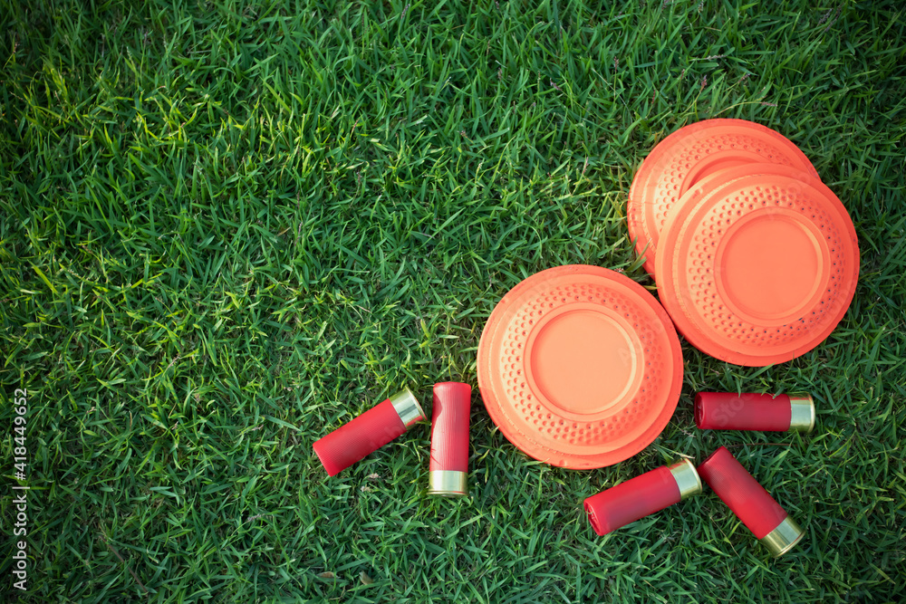 Clay disc flying targets and shotgun shells on green grass background ...
