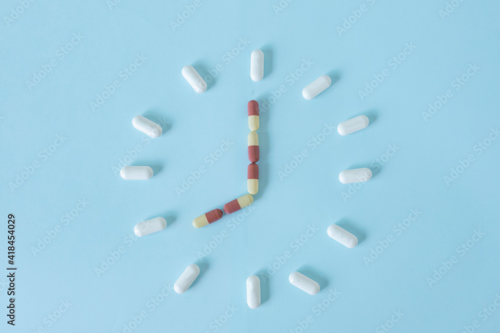 Clock created from white pills on pastel blue background. Right time ...