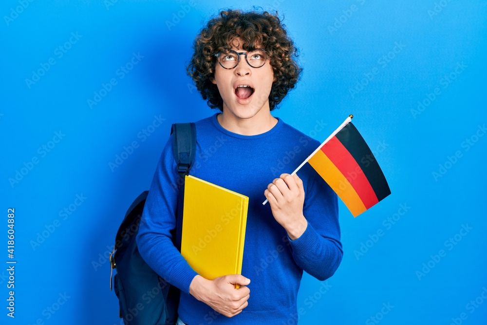 Handsome young man exchange student holding germany flag angry and mad ...