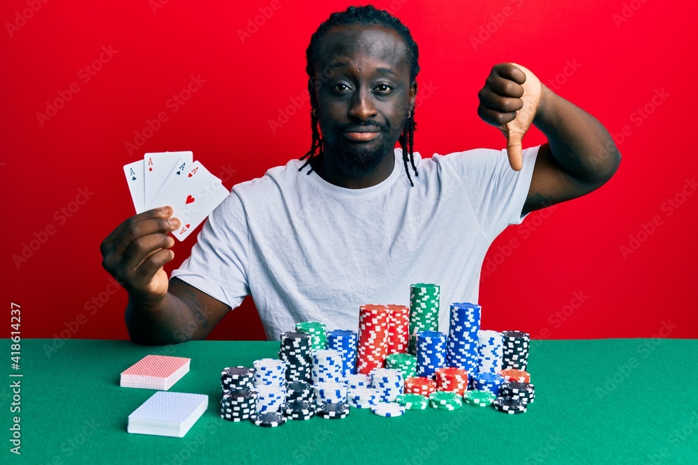 Handsome young black man playing poker holding cards with angry face ...