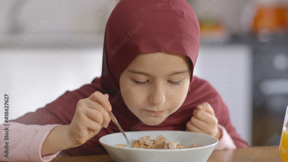 Breakfast in the kitchen. Portrait of muslim girl in hijab eating ...