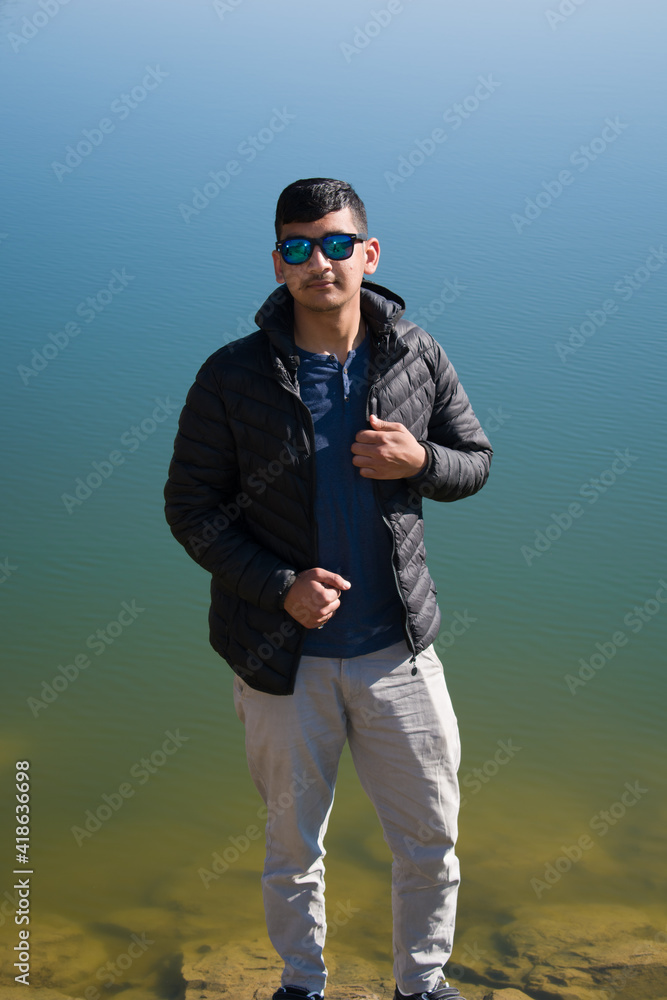 boy model standing on shore of lake wearing black jacket and sunglasses ...