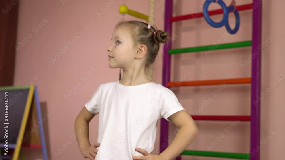 A little girl in a white T-shirt performs an exercise, turning her head ...