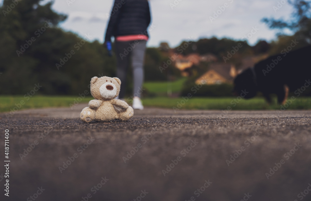 Lost Teddy bear doll sitting on footpath with blurry dog and women ...