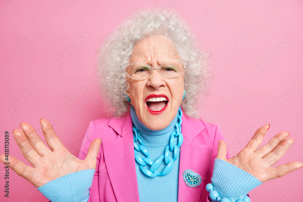 Disappointed elderly curly woman raises palms exclaims loudly expresses ...