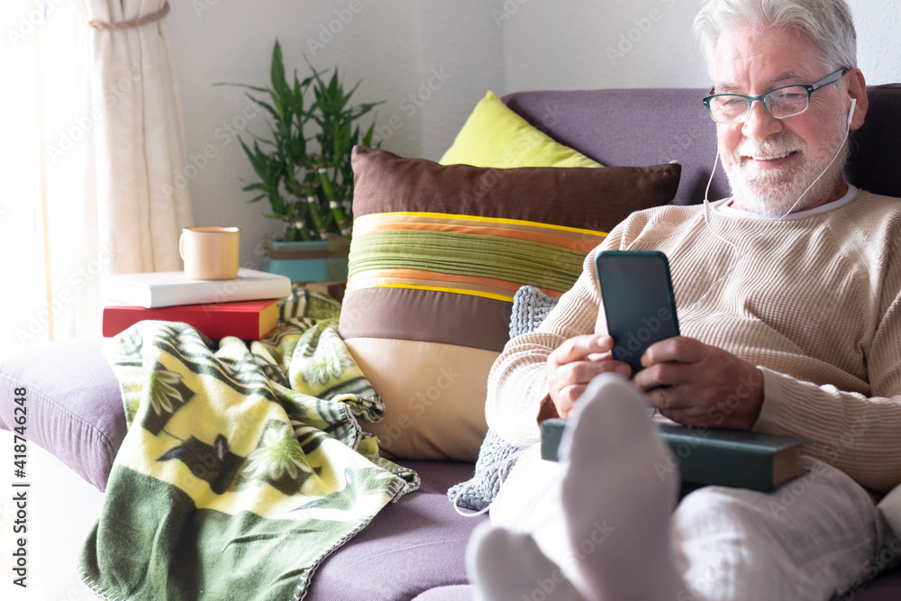 An elderly man with a white beard relaxes at home lying on the sofa ...