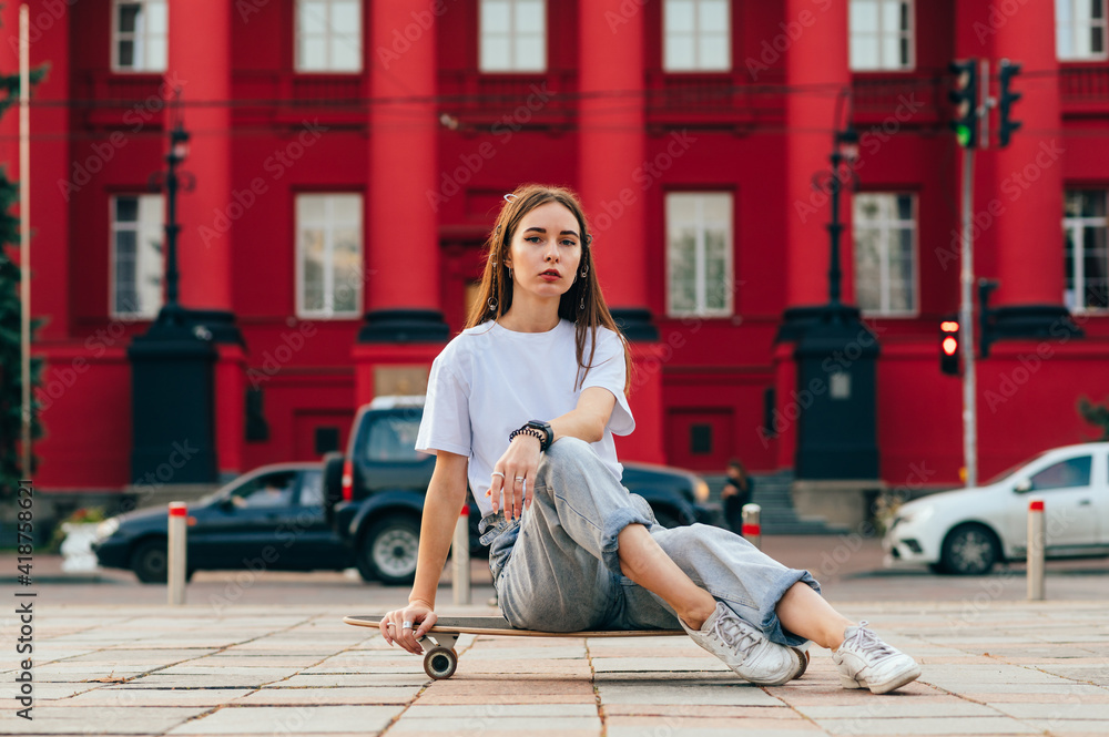 Relaxed beautiful young female skater is sitting on her skateboard ...