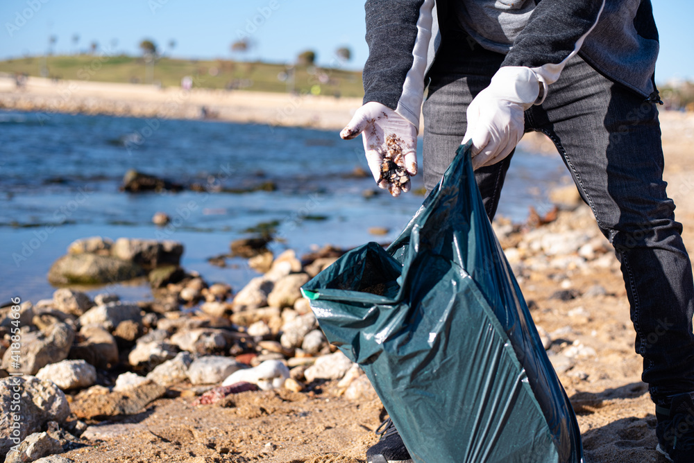 Man collects hazardous garbage in bag. Oil spill from tanker in sea or ...