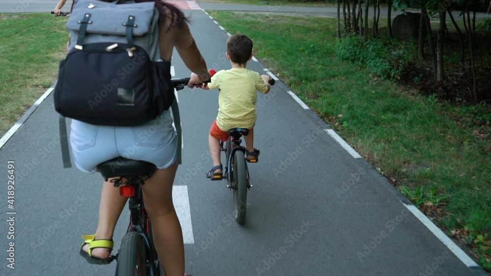 Little boy riding bicycle, parents on bikes behind him. Back view of ...