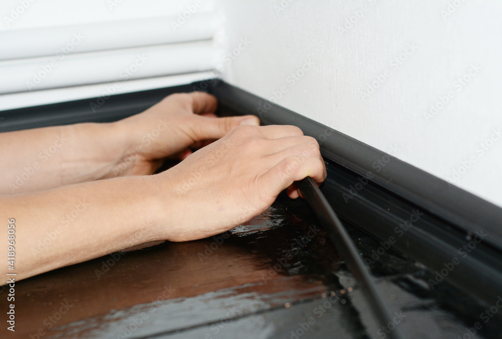 Foto de A man is installing a black plastic skirting board to hide ...