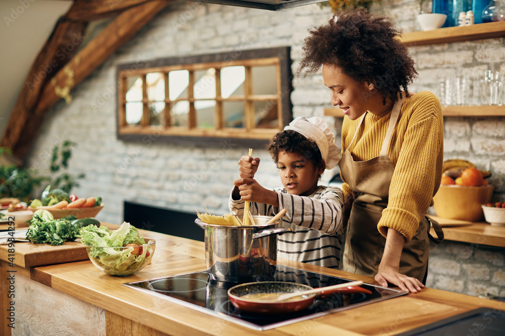 Small black boy cooking spaghetti with his mother in the kitchen. Stock ...