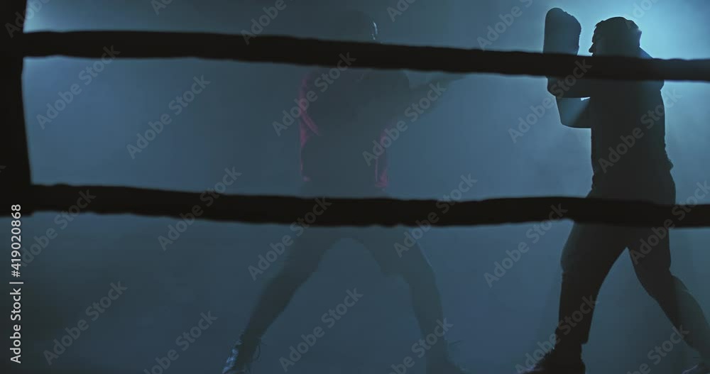 Dark ring in smoke, male trainer practicing punches with a professional ...