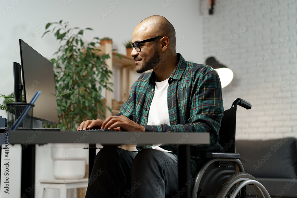 Disabled young african american man in wheelchair using computer while ...