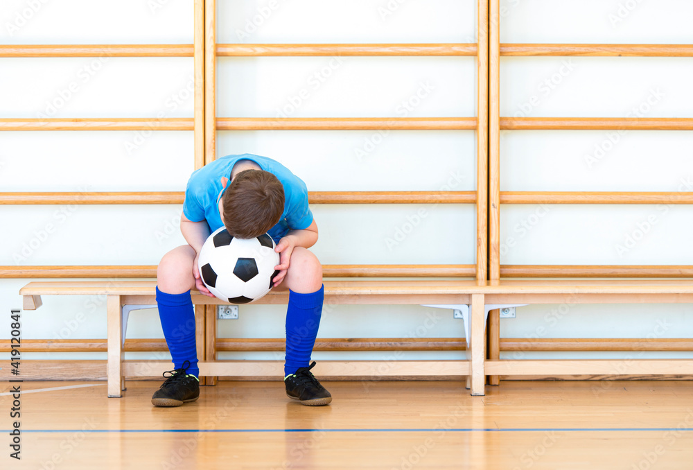Sad disappointed boy with soccer ball in a physical education lesson ...