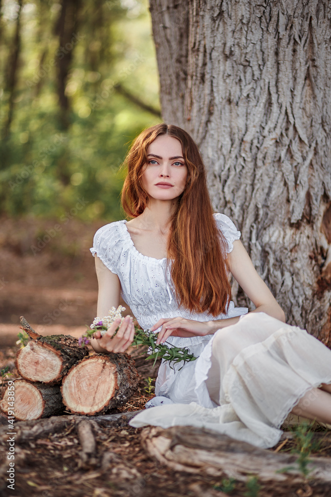 Red-haired peasant girl sitting on the ground in the forest. Red-haired ...