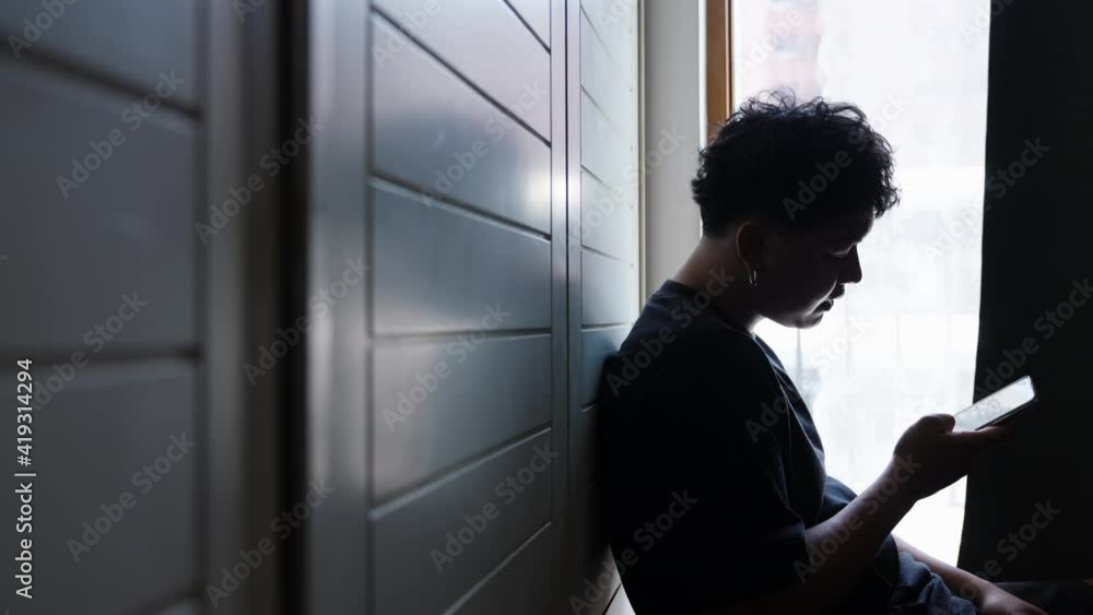 4K Depressed Asian man sitting by the window in bedroom with using ...