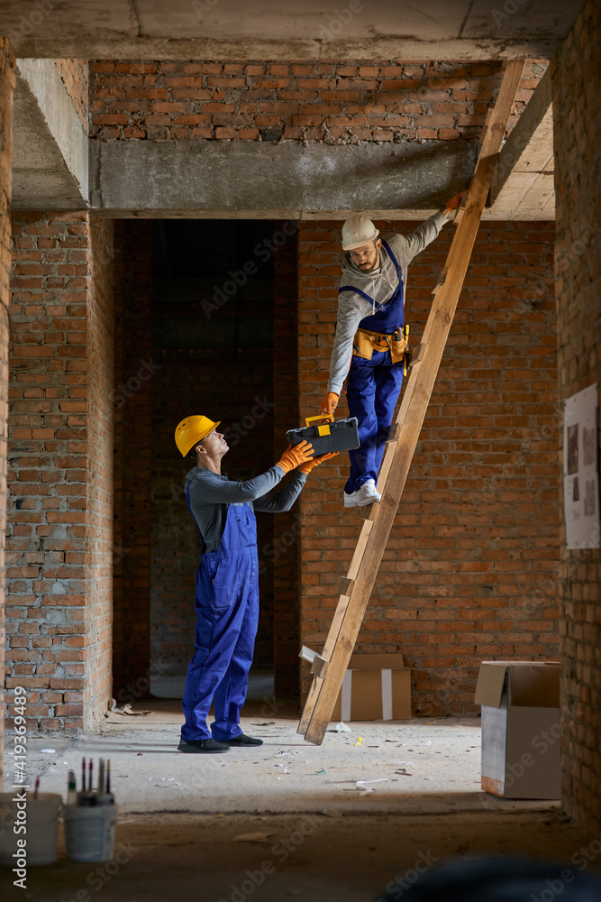Help. Full length shot of young workman in blue overalls and hard hat ...
