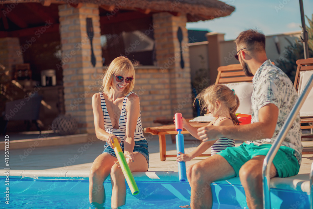 Parents playing with their daughter by the swimming pool, splashing ...