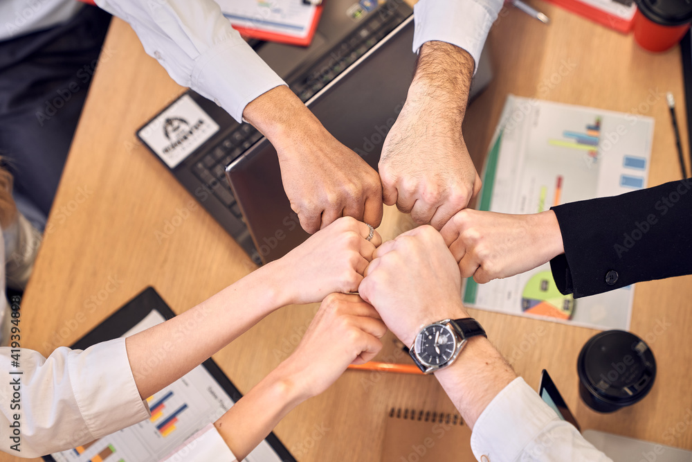Top view of cheerful business team keeping fists together as a symbol ...