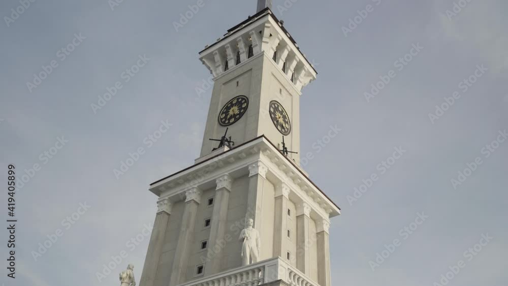 Bottom view of a clock tower with a long spire on blue cloudy sky ...
