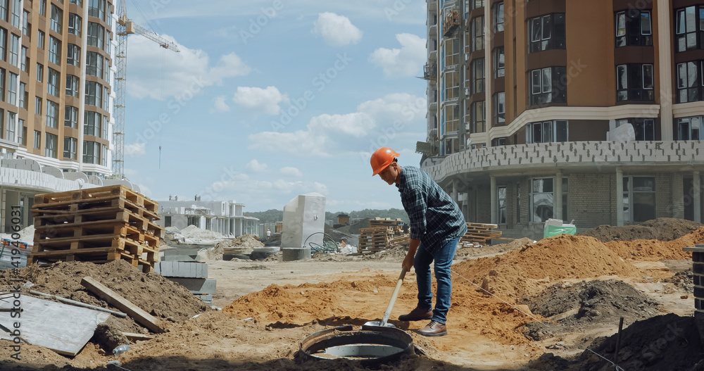 middle aged builder in hard hat digging ground with shovel on ...