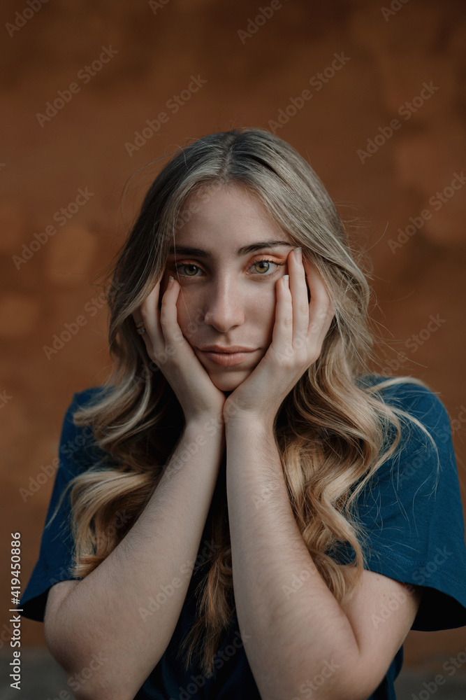 Young bored female with wavy hair touching face while looking at camera ...