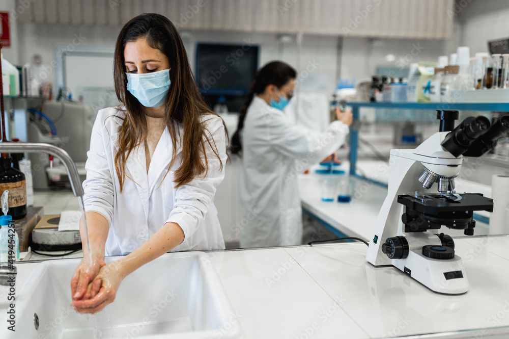 Female scientist in white coat and protective masks washing hands ...