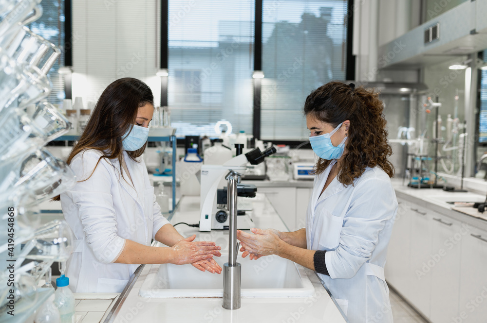 Side view of female scientists in white coats and protective masks ...