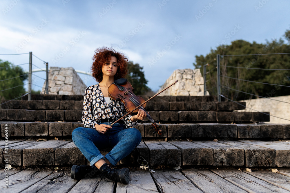 Full body young pretty female musician in casual wear sitting with ...