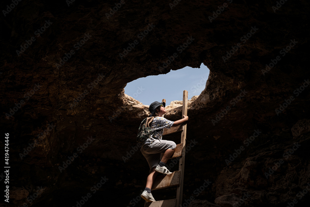 Boy exploring a cave while climbing stairs through a hole Stock Photo ...