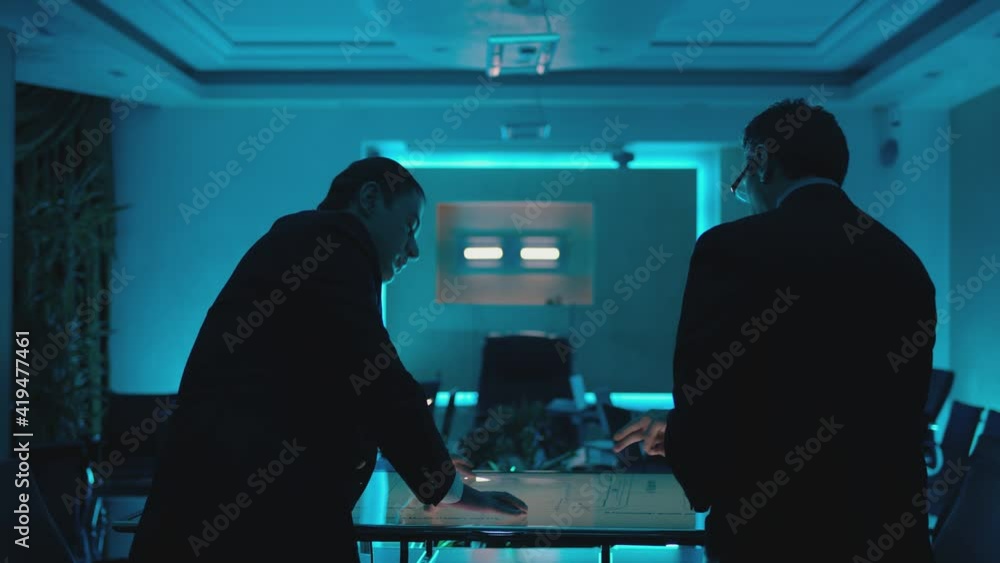Two men in black suits meeting at dark office room and using a modern ...