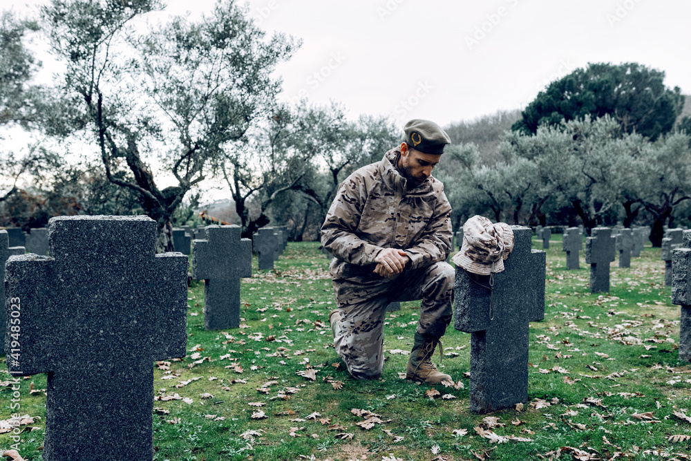 Full body sorrowful soldier in camouflage outfit kneeling down in front ...