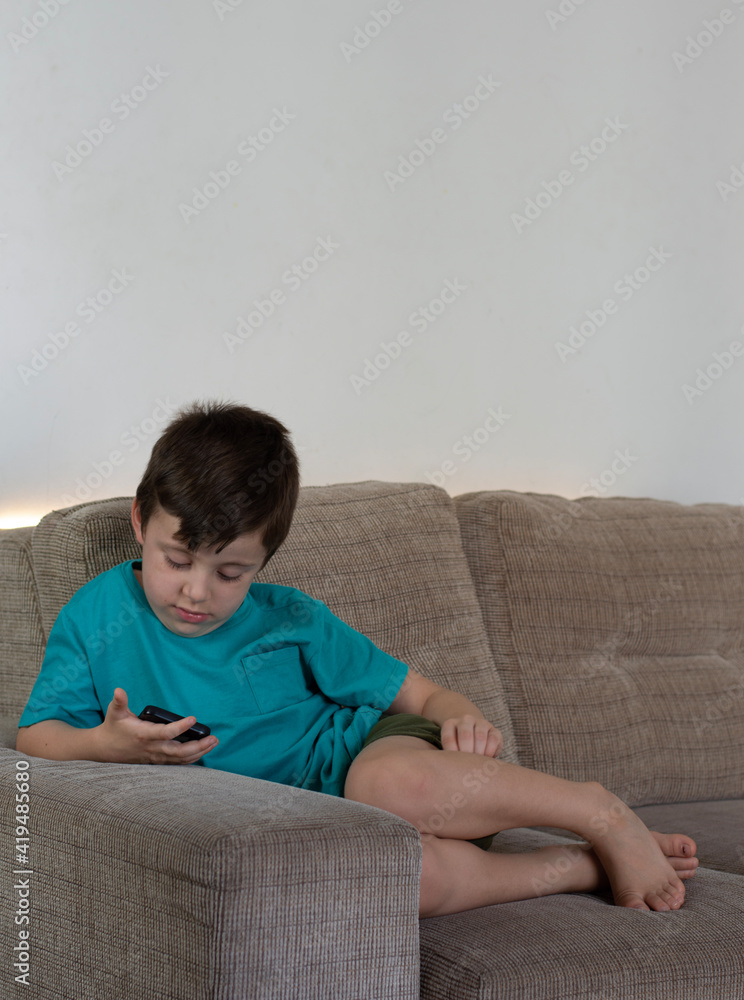 Cute little boy barefoot using a smartphone, looking at the screen ...