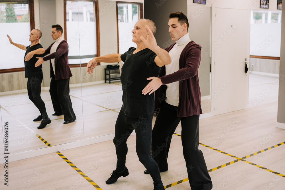 Side view of male instructor helping mature dancer with movement during ...