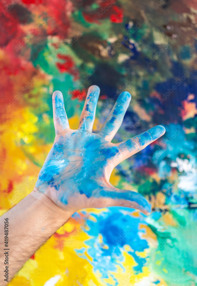 Artist with open hand showing palm with blue paint near colorful canvas ...