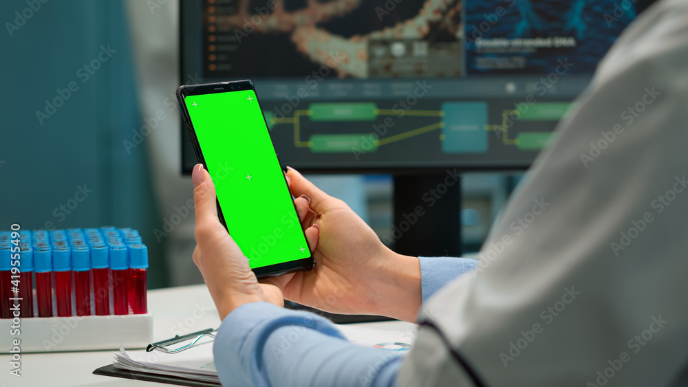 Medic in scientific laboratory holding phone with greenscreen wearing ...